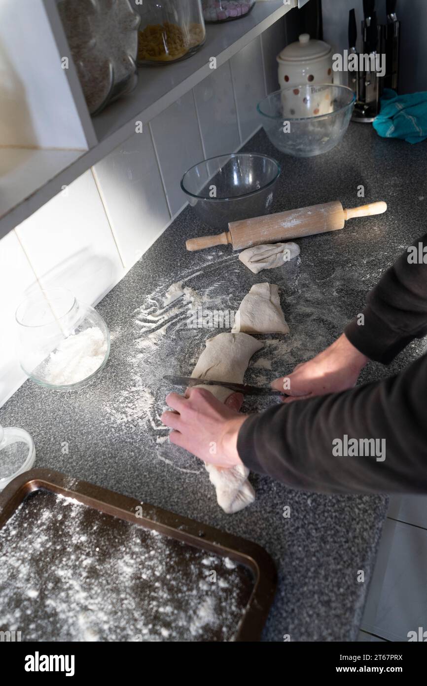 Teenage boy making bread and cutting the bread dough with a palette ...