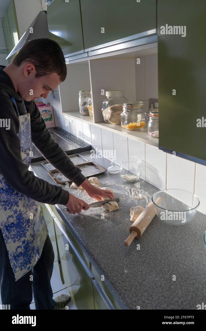 Teenage boy making bread and cutting the bread dough with a palette ...