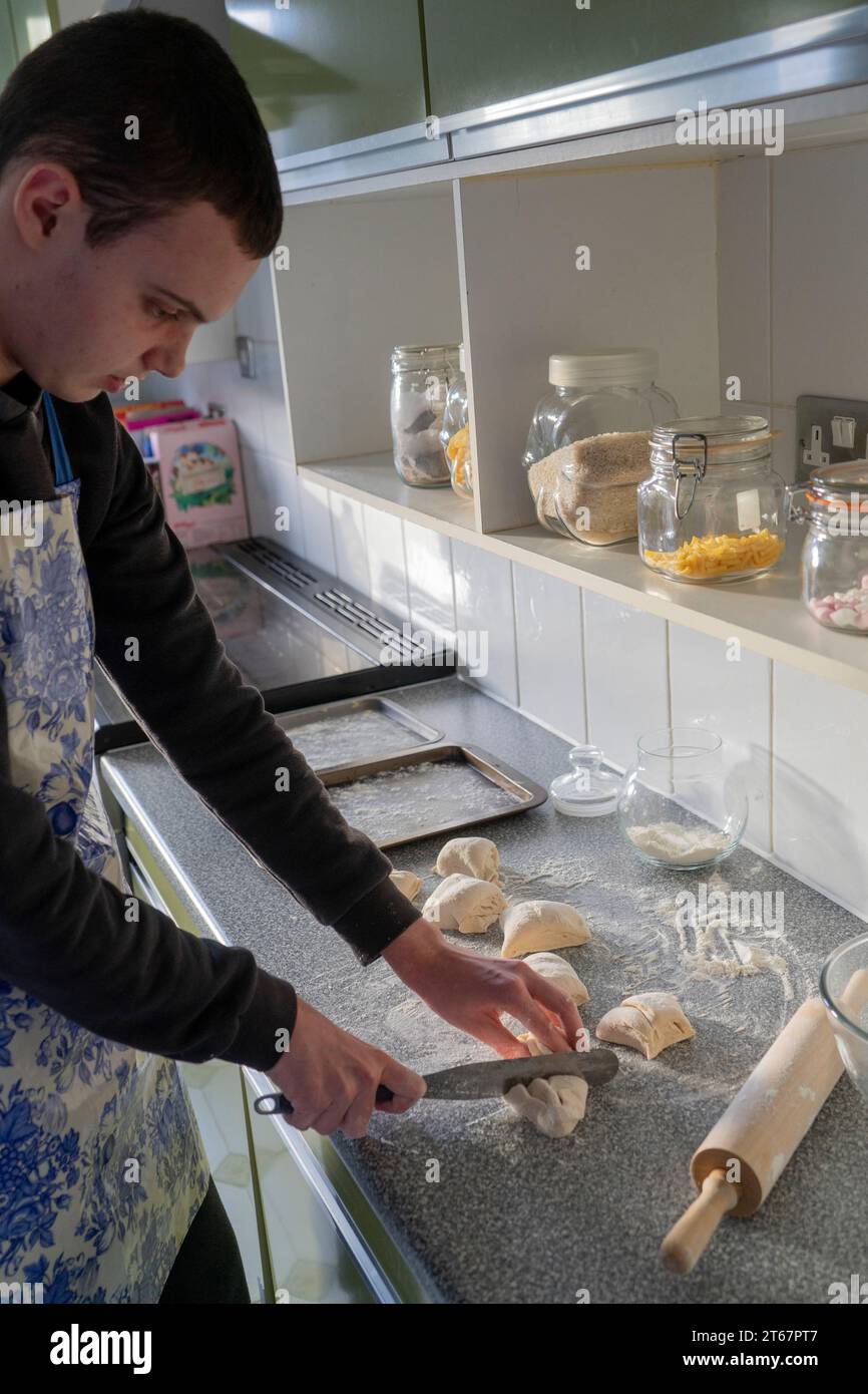 Teenage boy making bread and cutting the bread dough with a palette ...