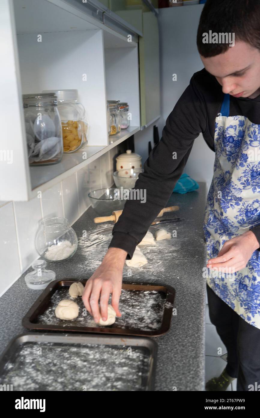 Teenage boy making bread rolls in the kitchen at home wearing an apron ...