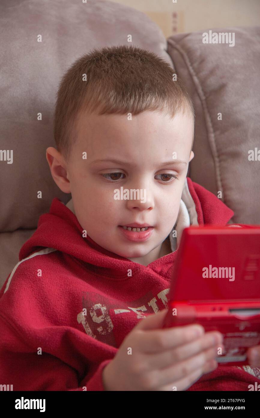 Young boy wearing a bright red hoody top sitting on a beige sofa and ...