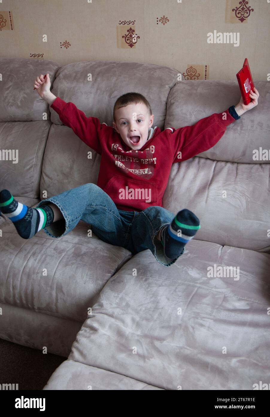 Excited young boy wearing a bright red hoody top and playing with a red ...