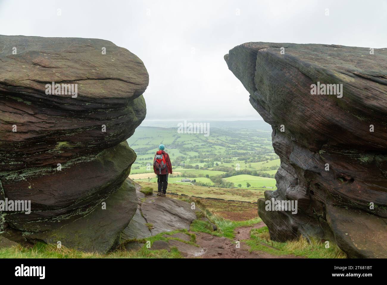 A walker standing between eroded rocks in The Roaches, Staffordshire ...