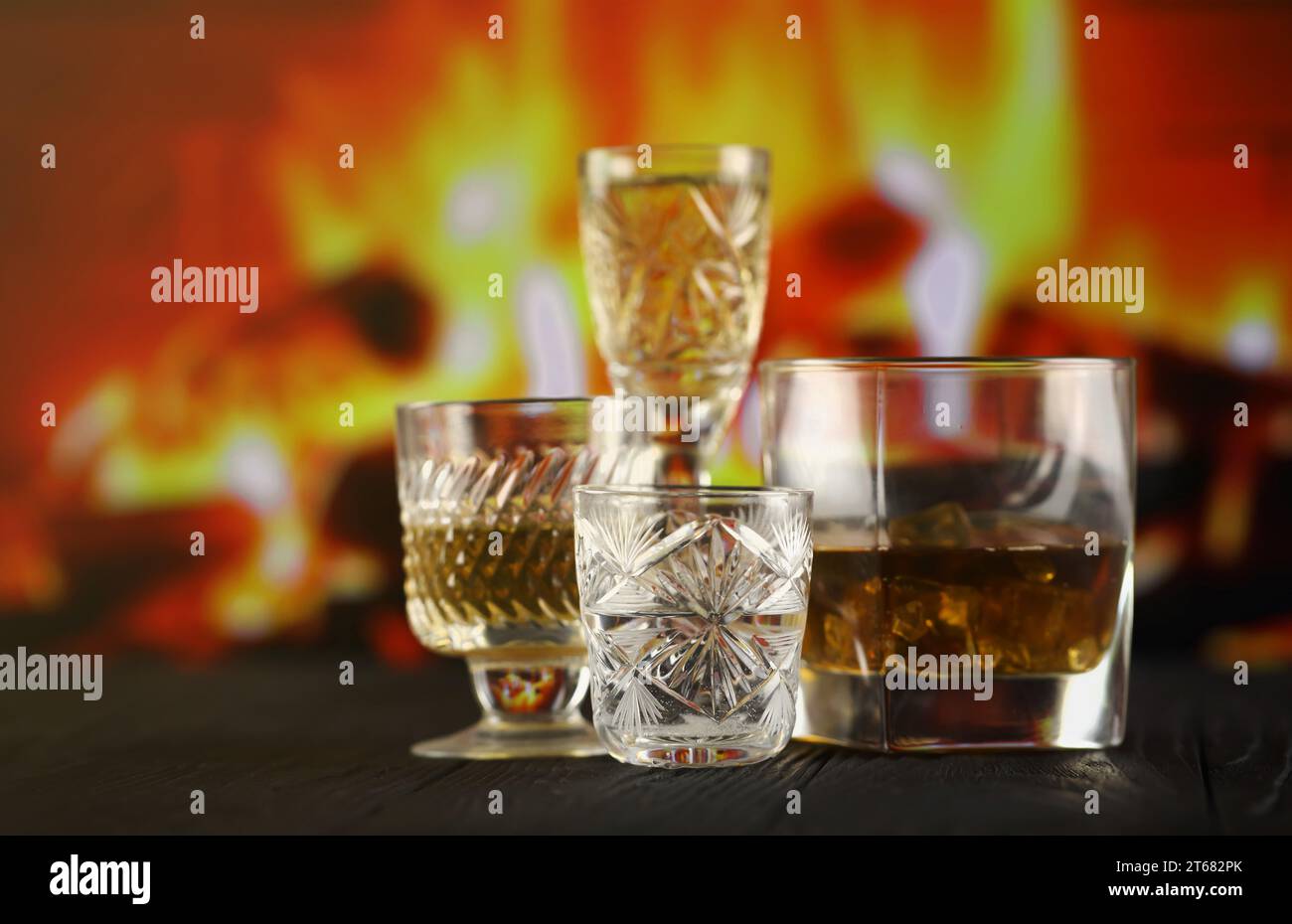 Different alcohol drinks in glass on wooden surface on fireplace ...