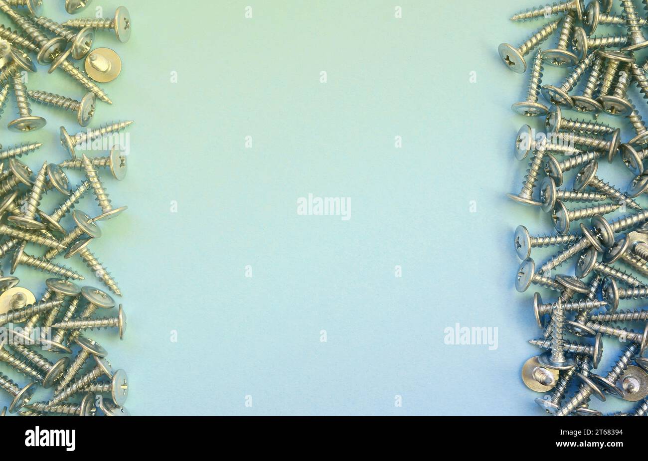 A lot of small silver screws lies on a light blue background. Minimal ...