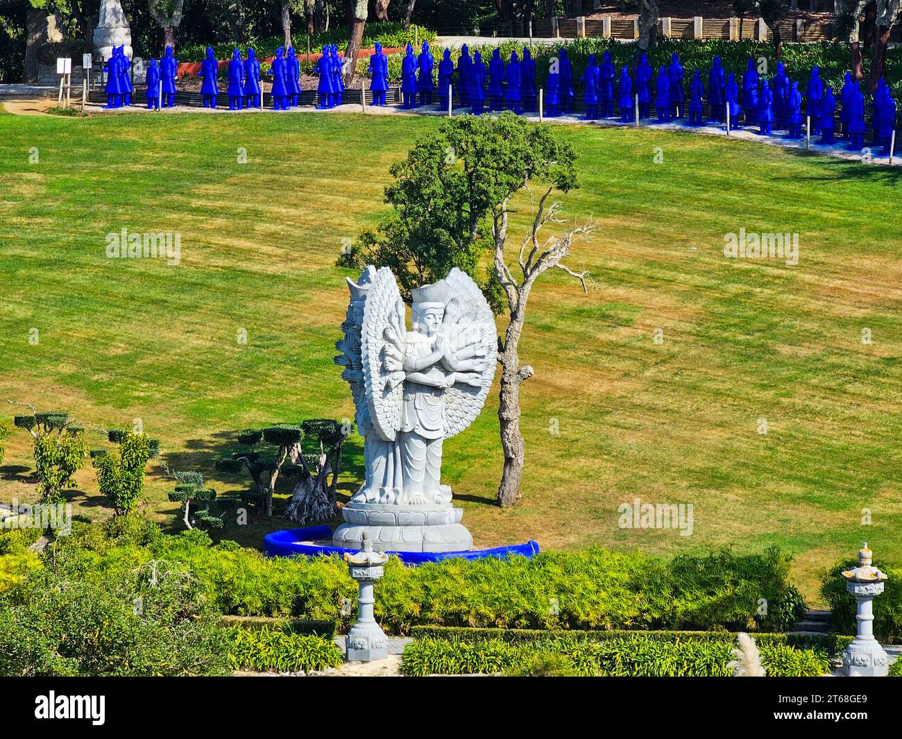 A majestic garden statue of an angel stands amidst vibrant foliage, a ...