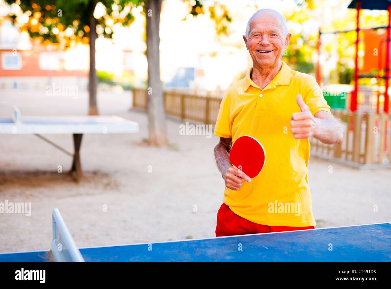 Portrait of elderly man with rackets for table tennis showing thumb up ...