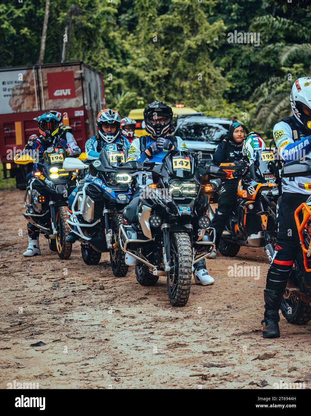 A group of motorcyclists are gathered in a dusty area, lined up in a ...