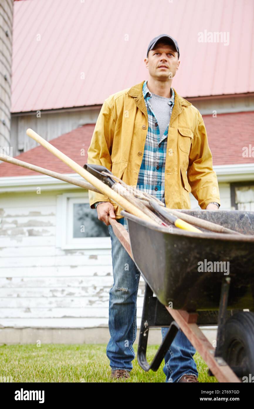 I work hard. A serious man standing outside with his wheelbarrow Stock ...