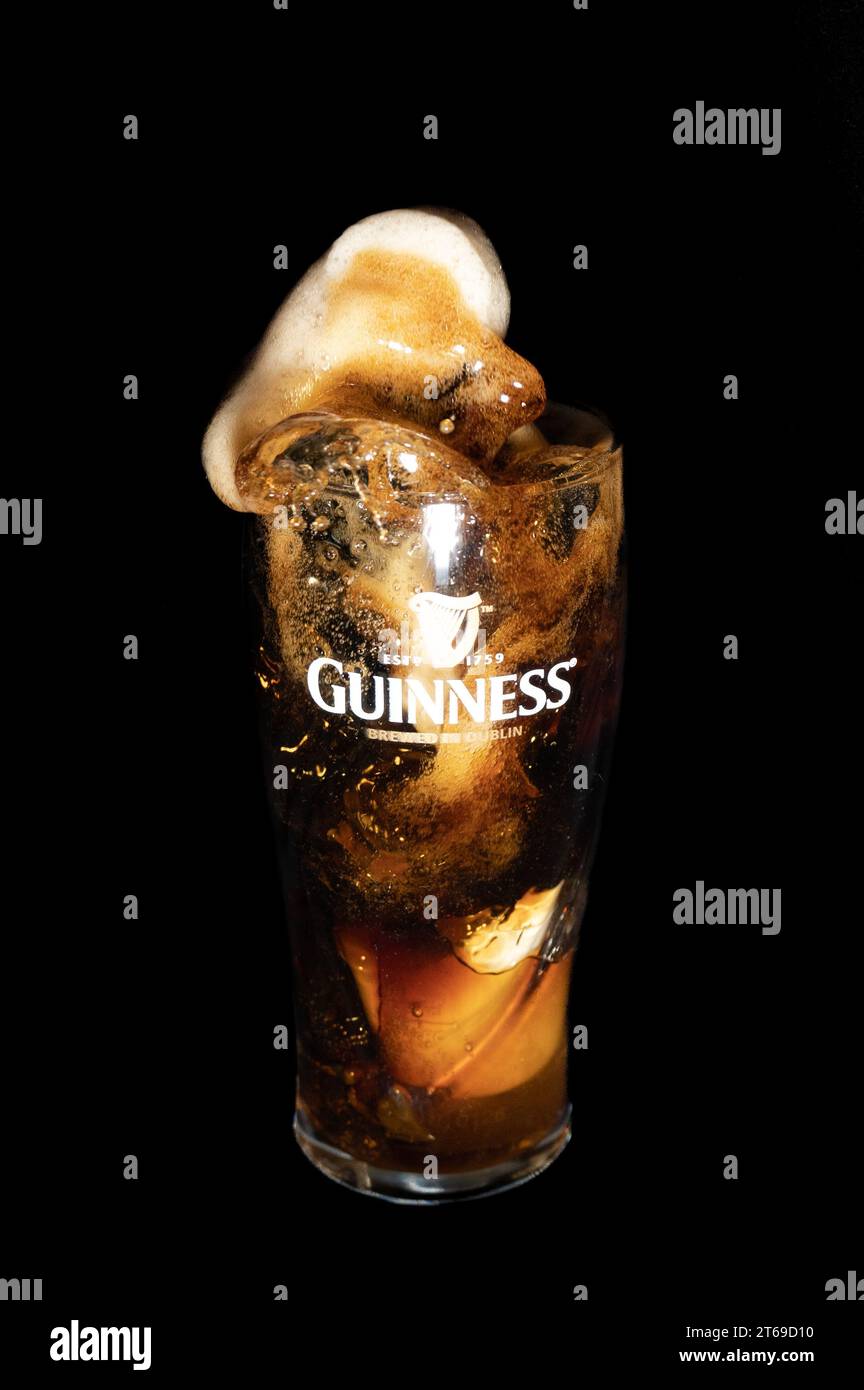 A vertical image of a dark brown, foamy Guinness beer drink on a solid ...