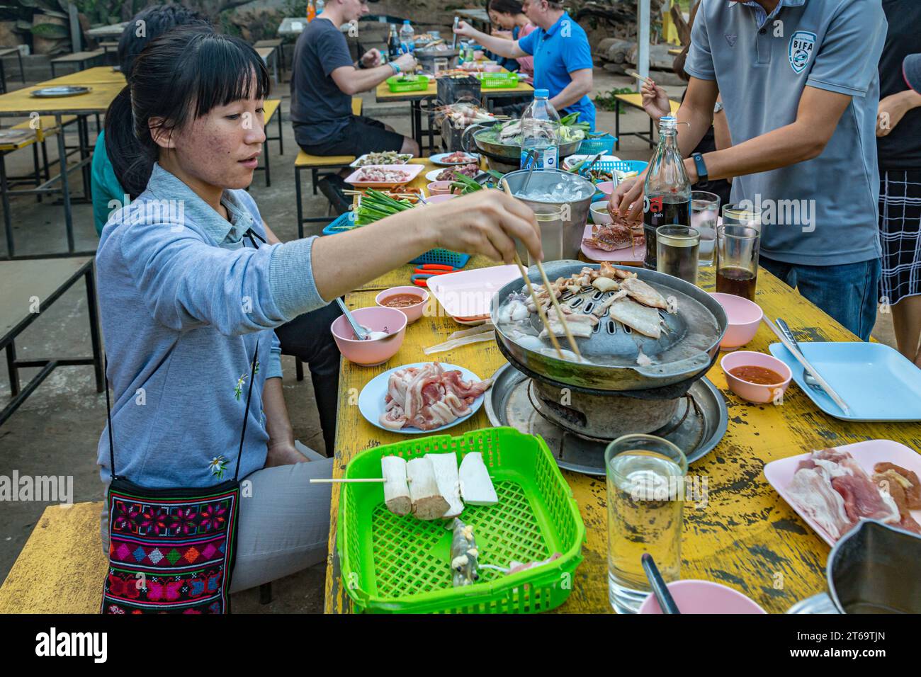 Thai woman cooking fish on a charcoal hot pot at a buffet style outdoor restaurant in Chiang Rai ...