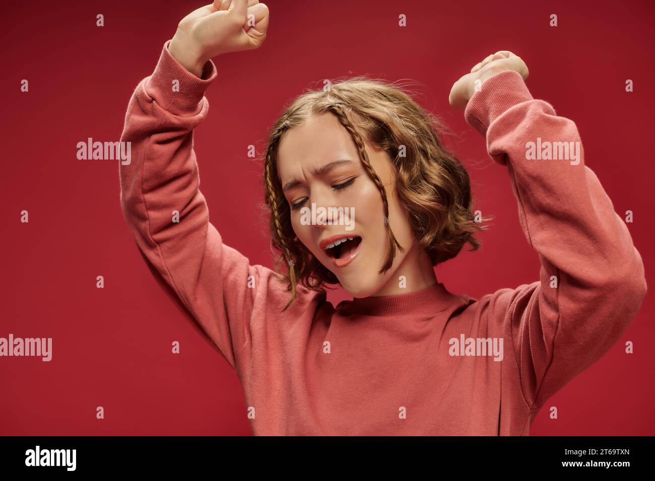 young gen z woman with short hair and braids posing with raised hands ...