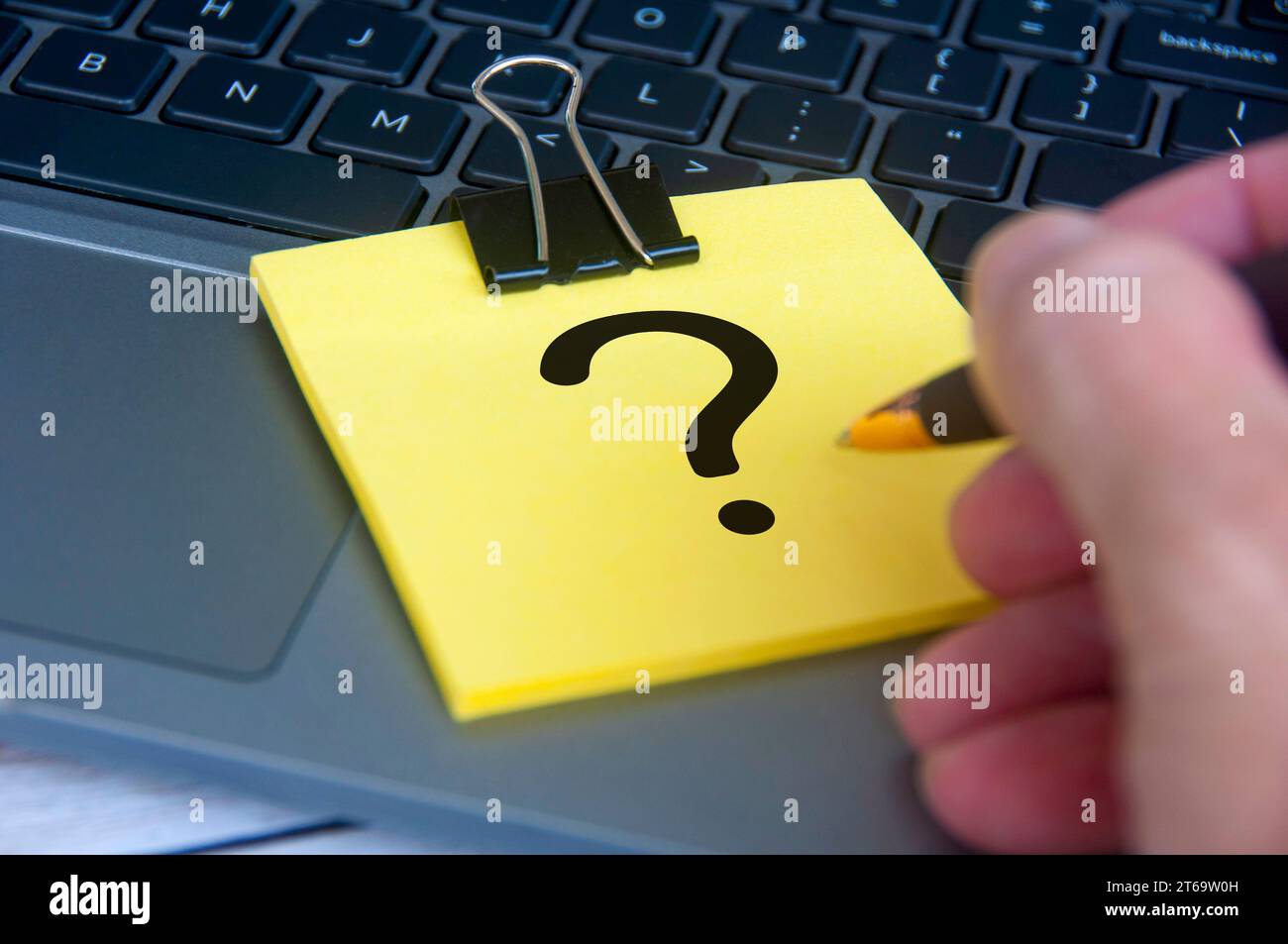 Question mark on yellow notepad with laptop background. Question and ...