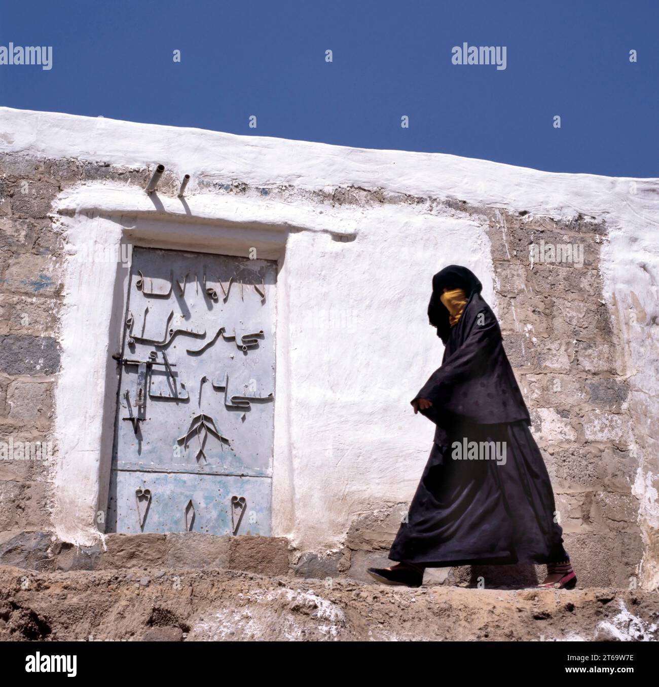 A veiled Muslim woman walks on a Sanaa street, Yemen.At background a ...