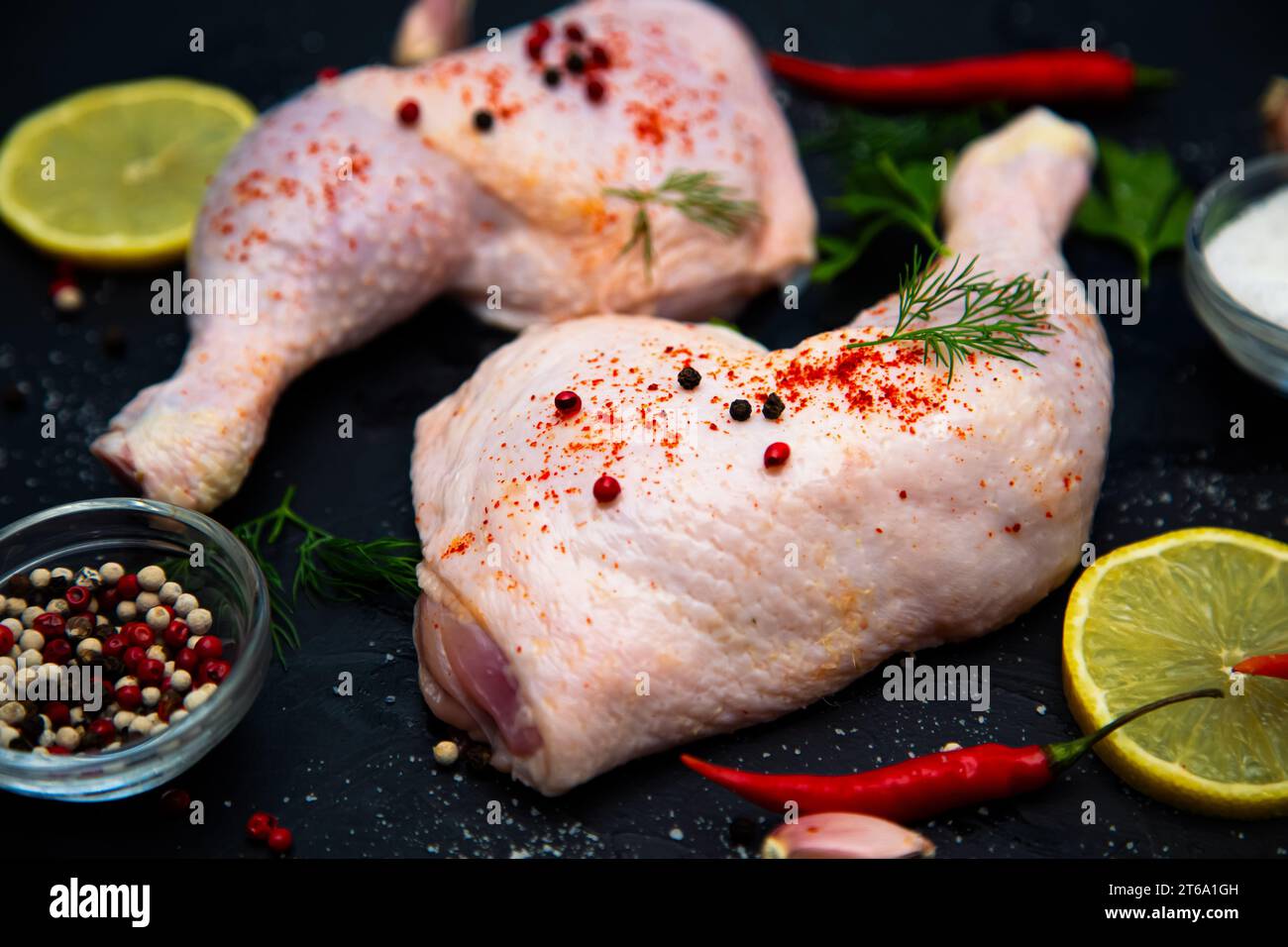Raw chicken legs, garlic, chili, lemon and herbs on a black background ...