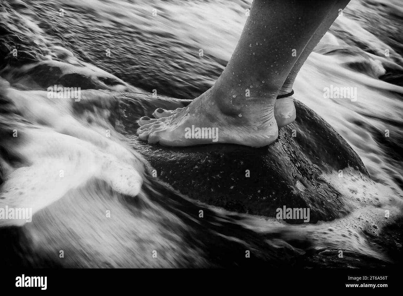 Black and white photograph of a person standing in the surf, with their ...