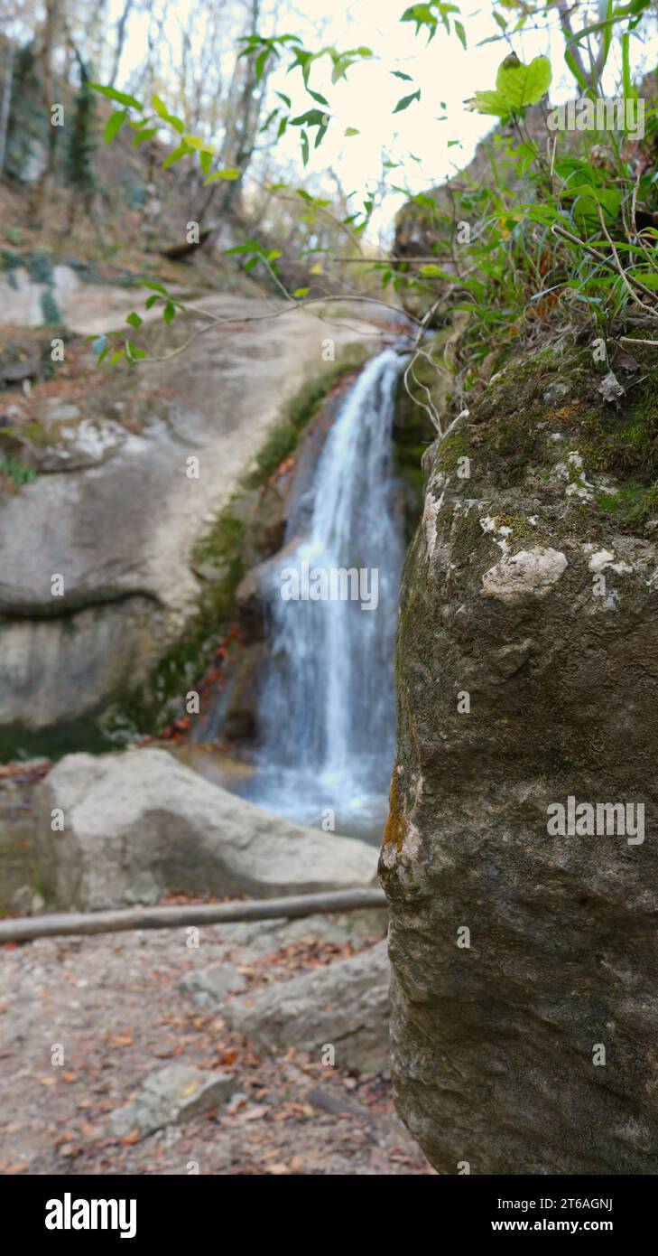 vertical image of a small waterfall in blurred focus visible from ...