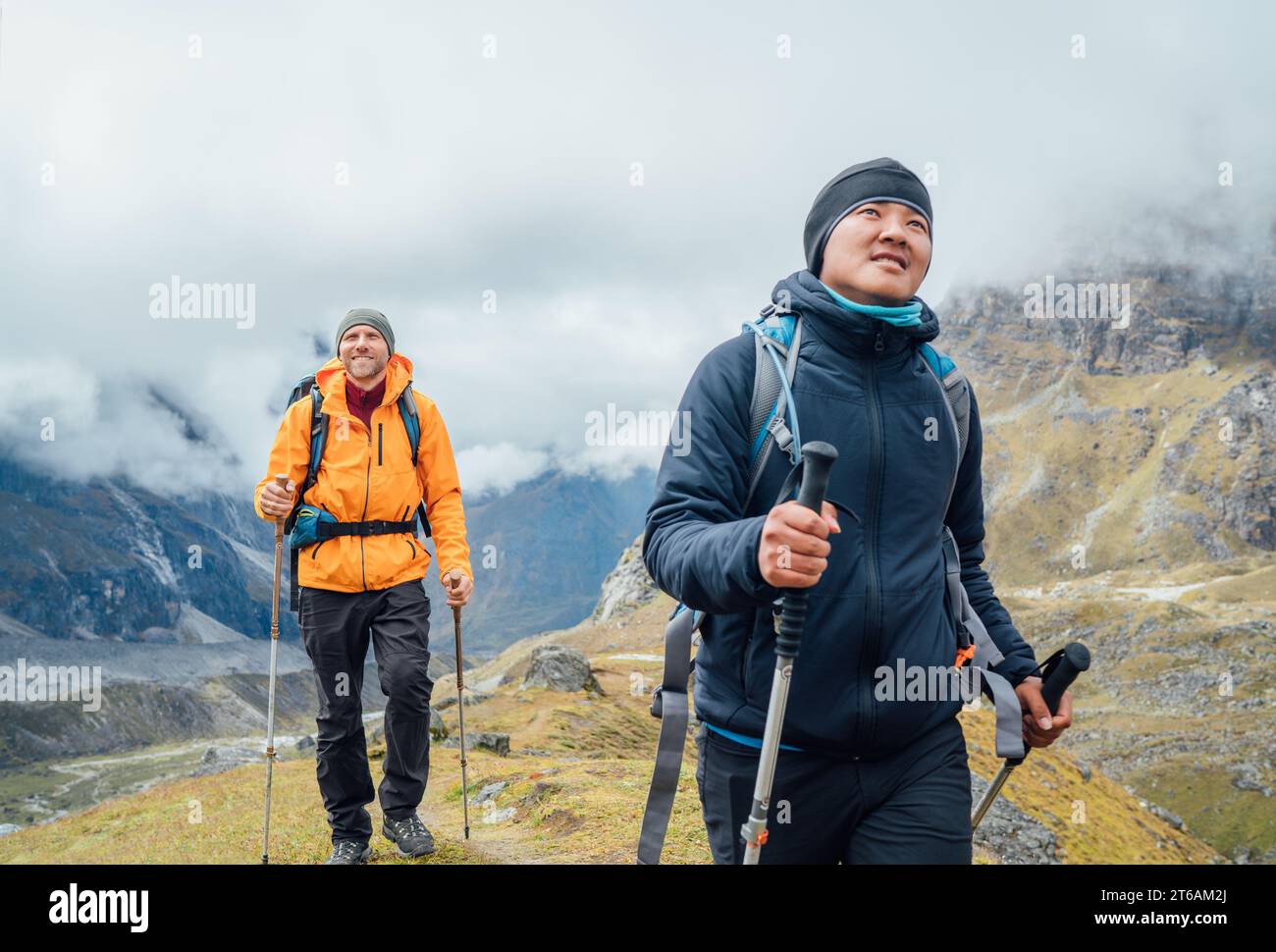 Caucasian and Sherpa men backpackers with trekking poles together ...