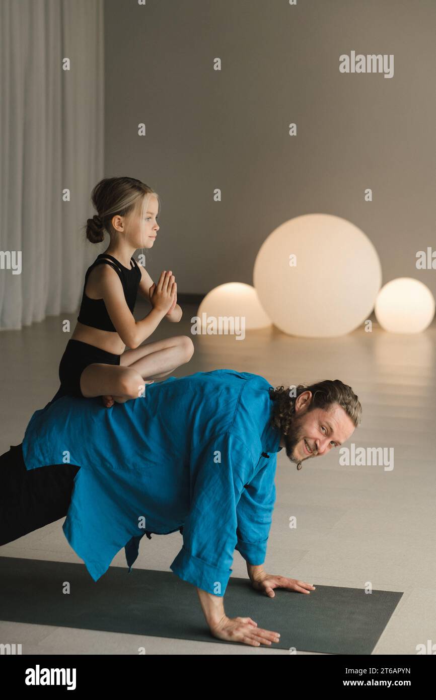 a child in the lotus position sits on the back of a yoga coach during ...