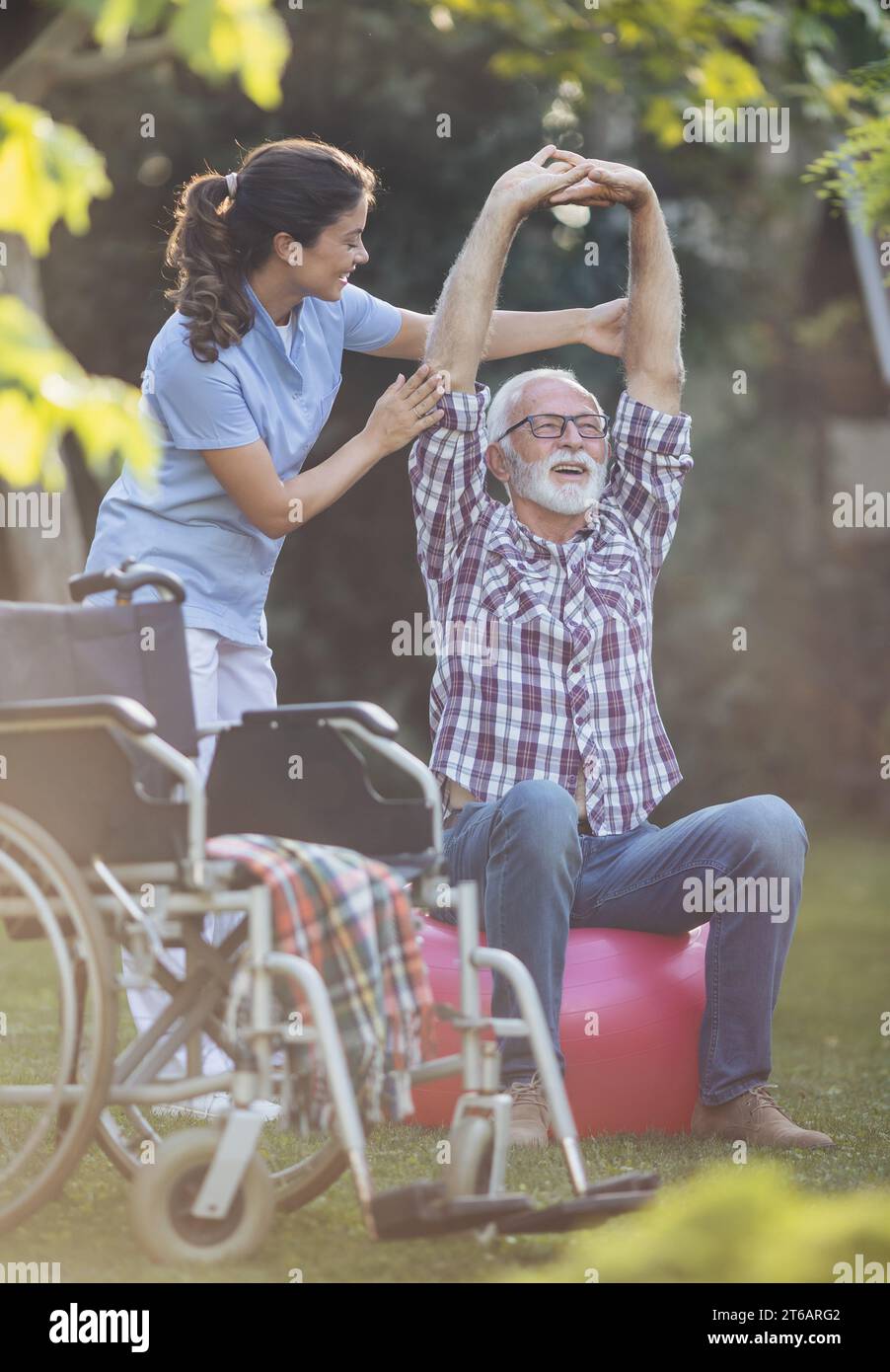 Young woman physiotherapist helping senior man with stretching painful ...