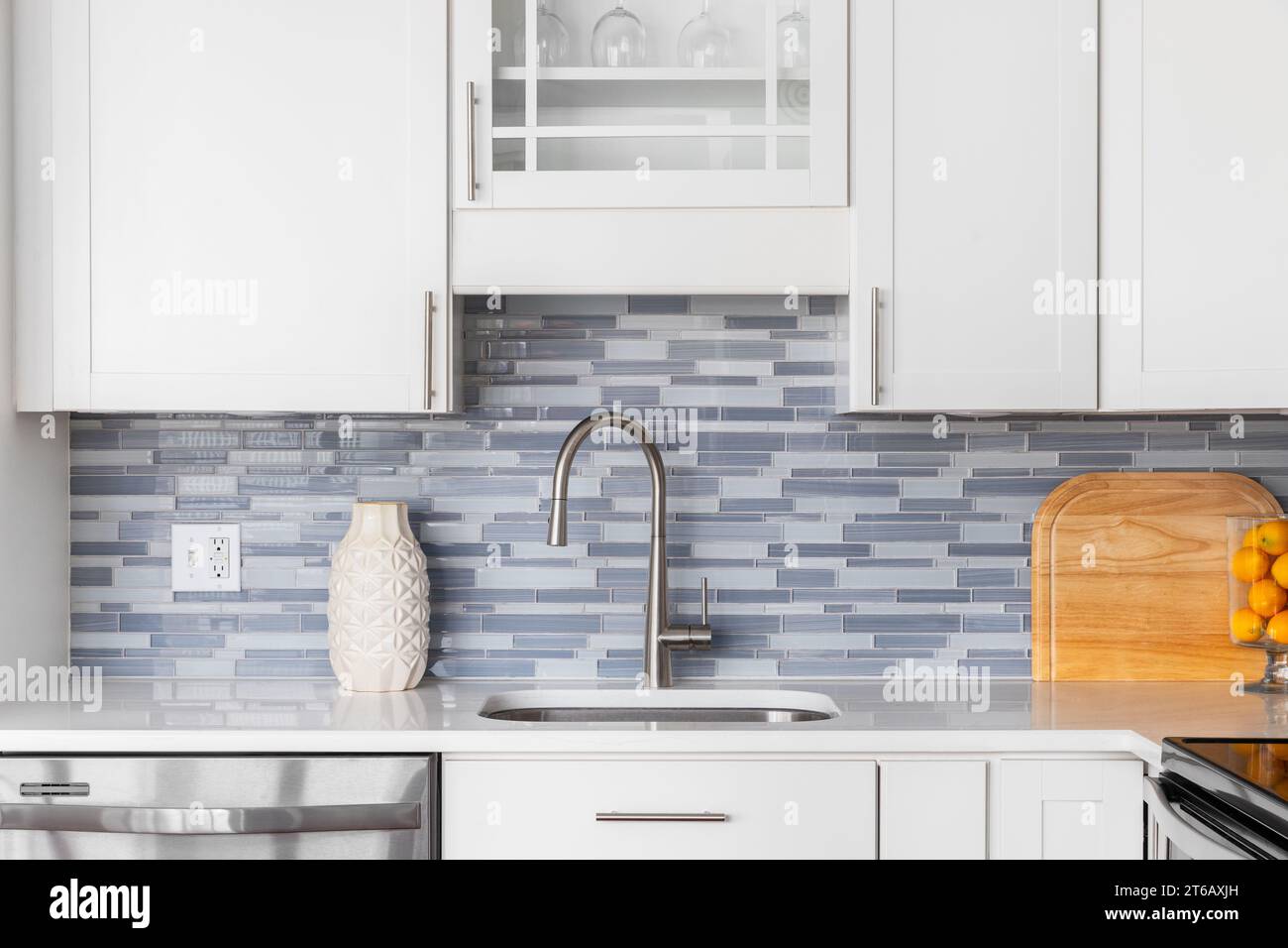 A kitchen faucet detail with a blue glass tile backsplash, white ...