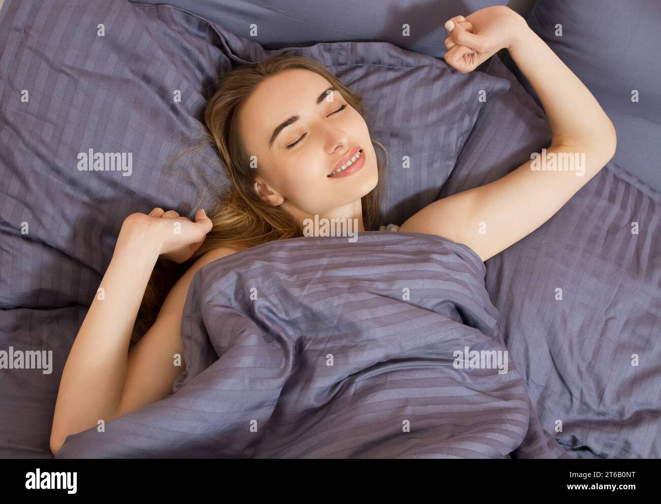 Beautiful young woman stretching after waking up while in cozy bedroom ...