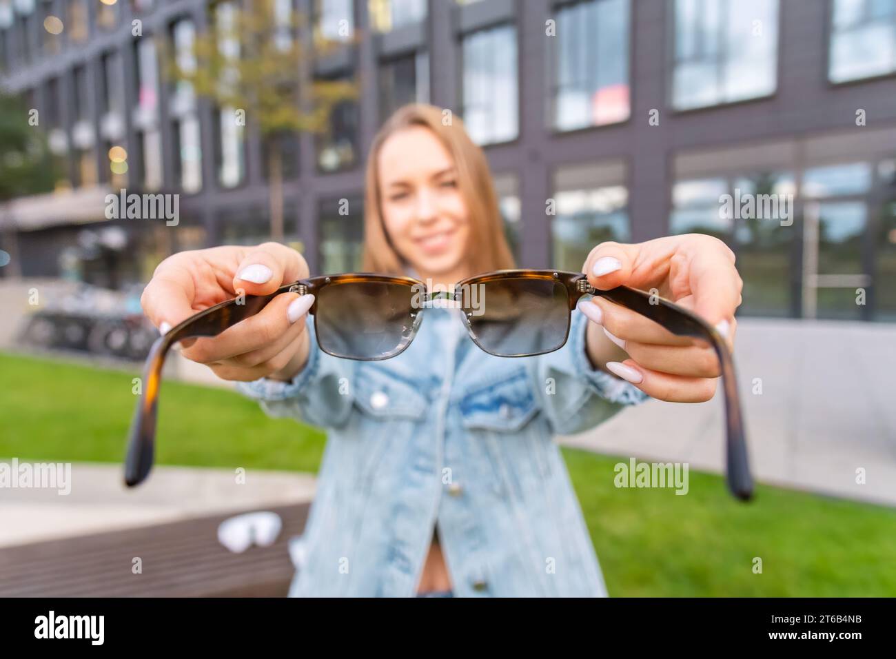 Young blonde woman holding eyeglasses standing near a modern building ...
