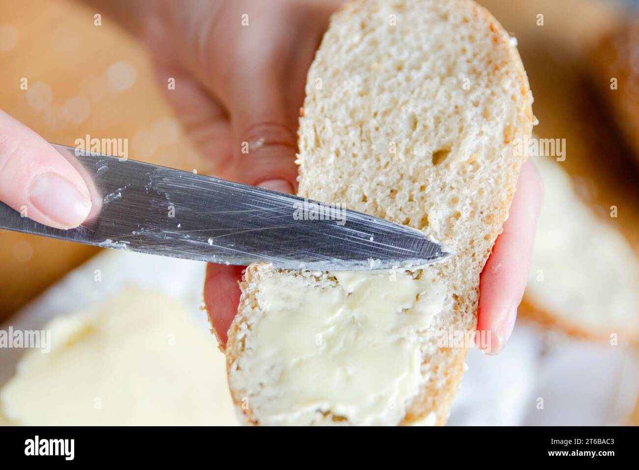 Close-up of woman's hands spreading butter on a slice of bread. Quick ...