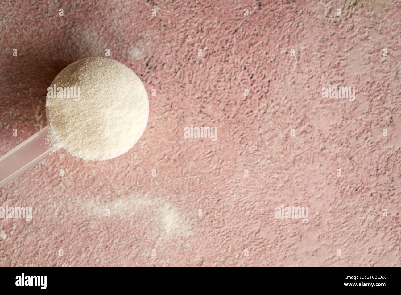 Collagen powder in a plastic measuring cup on pink background with copy ...