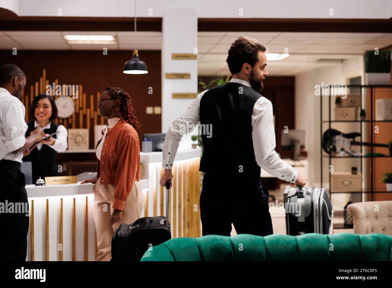 Hotel bellboy helping guests with bags, carrying luggage to room in ...