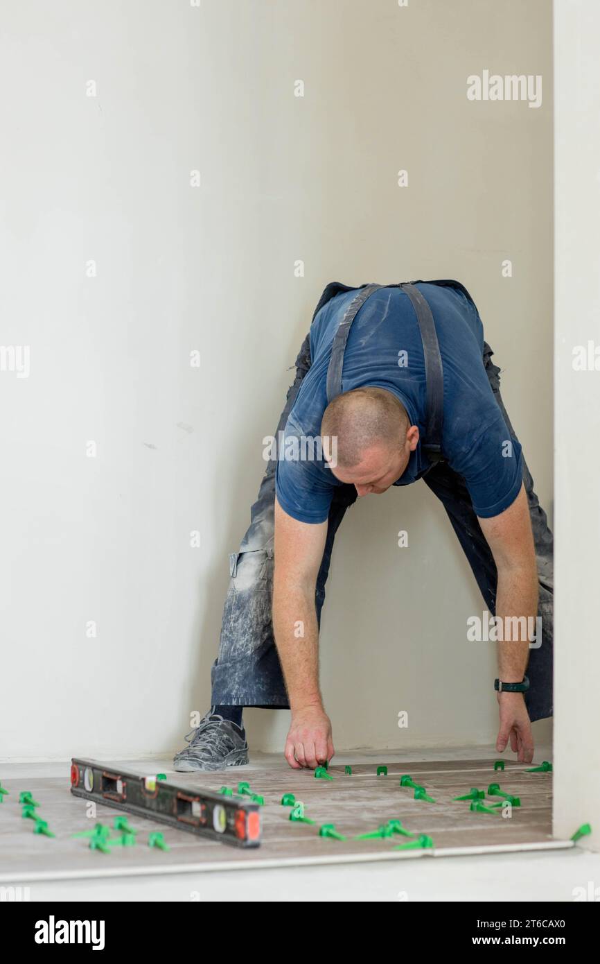Tiler placing ceramic wall tile in position over adhesive with lash ...