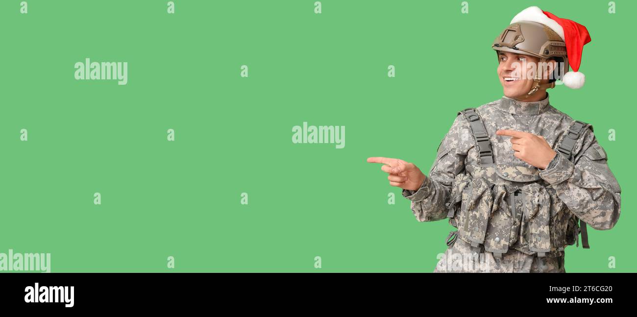 Soldier with Santa hat showing something on green background with space ...