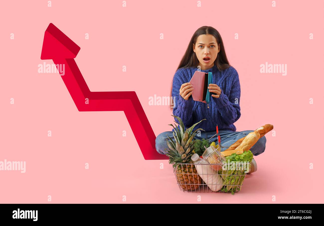 Shocked woman with empty wallet and shopping basket on pink background ...