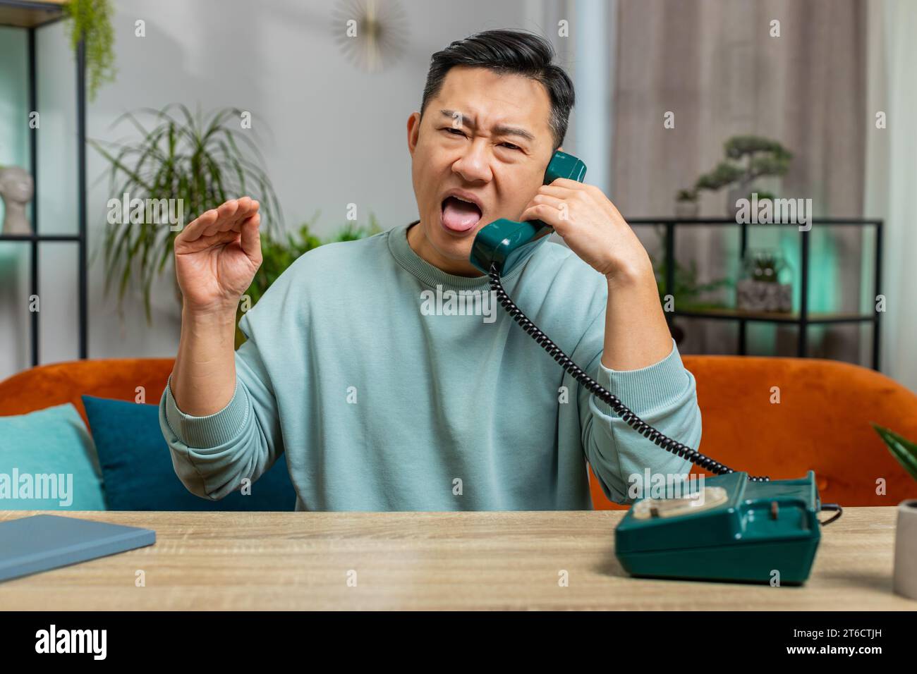 Tired bored Asian man talking on wired vintage telephone of 80s ...