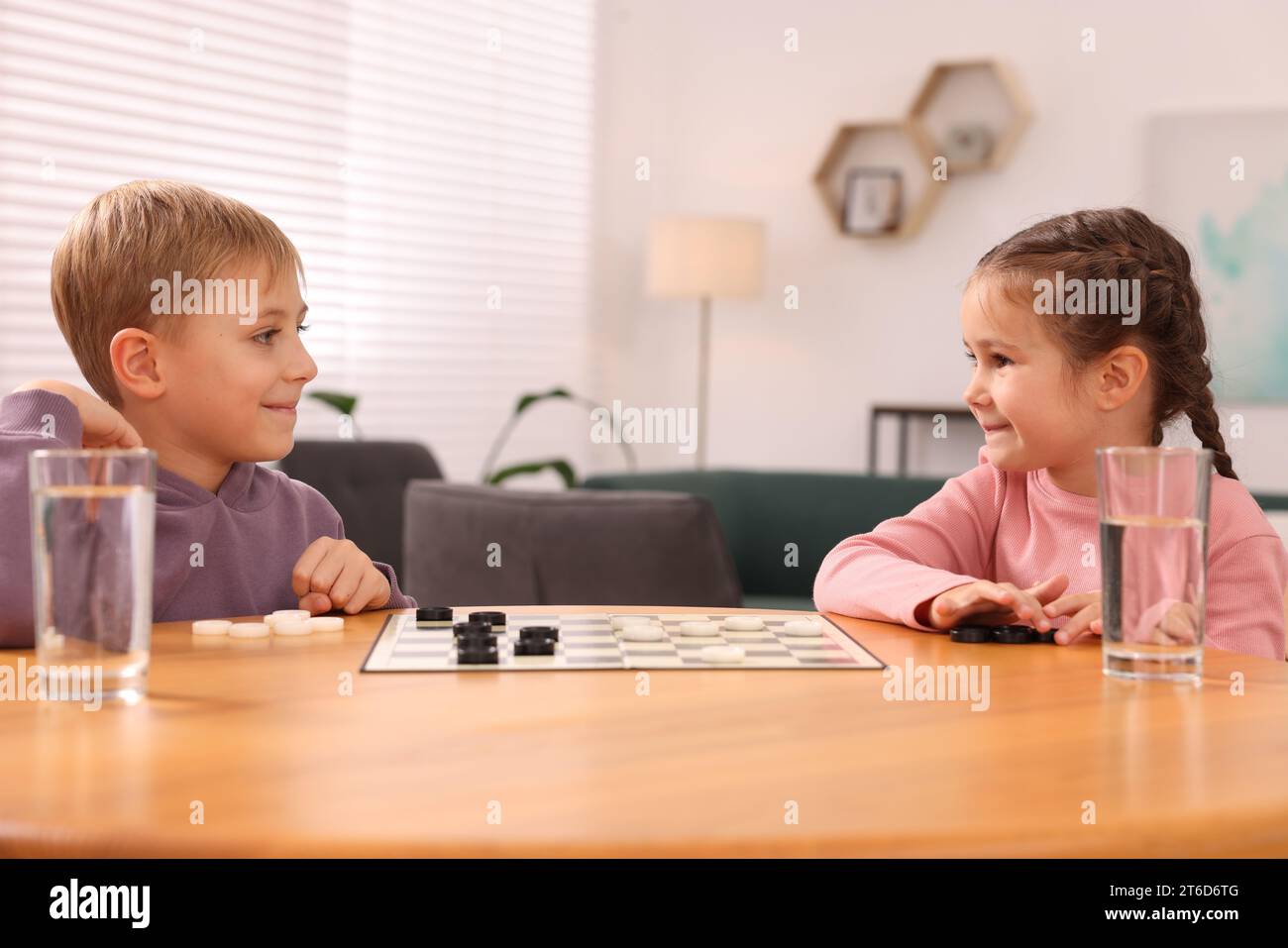 Cute children playing checkers at wooden table in room Stock Photo - Alamy