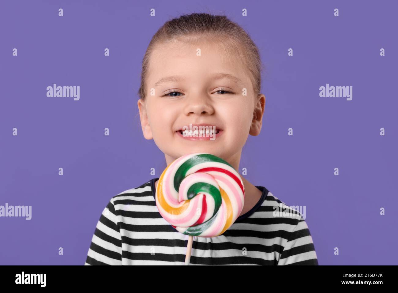 Happy little girl with colorful lollipop swirl on violet background ...