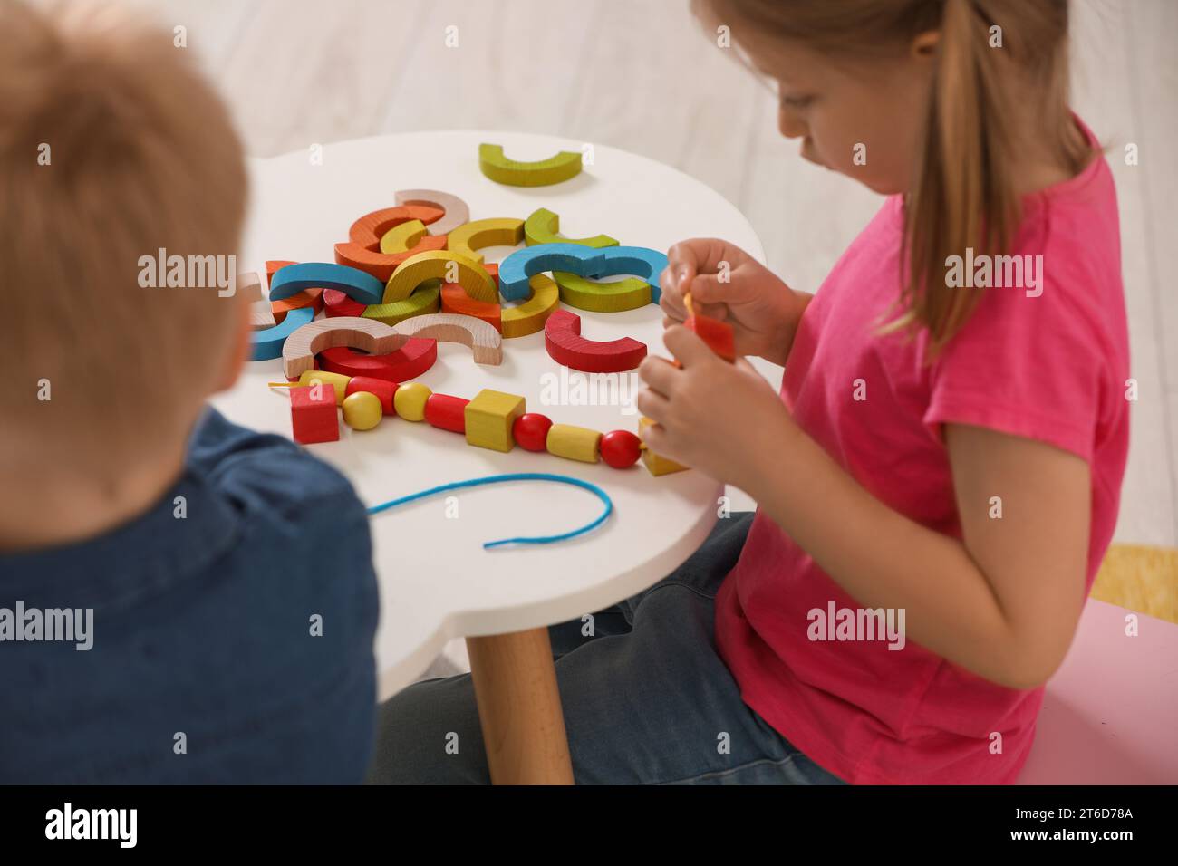 Little children playing with wooden pieces and string for threading ...