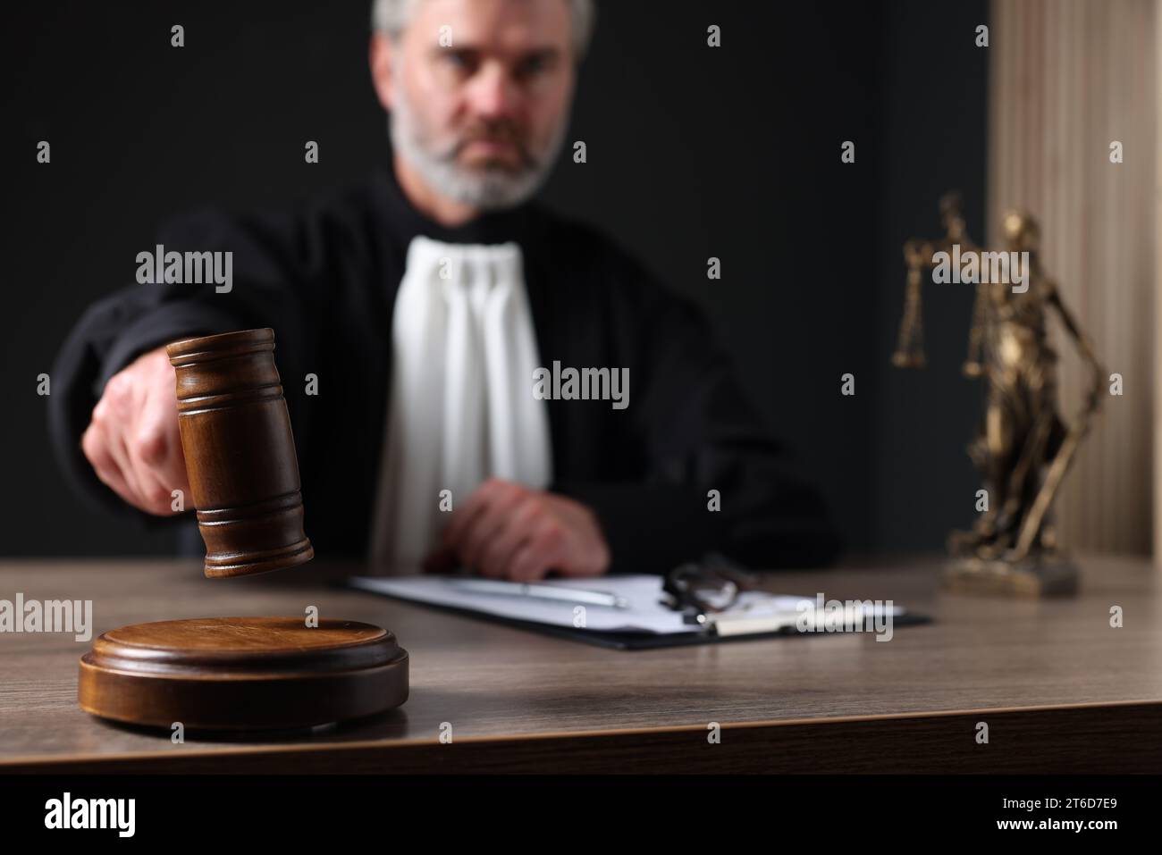 Judge with gavel and papers sitting at wooden table against black ...
