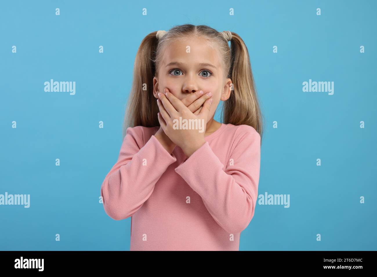 Embarrassed little girl covering her mouth with hands on light blue ...
