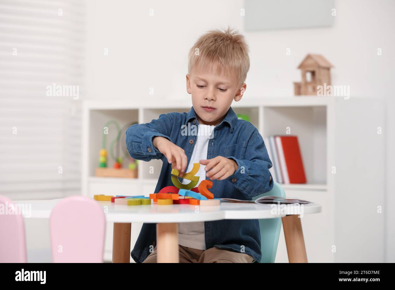 Cute little boy playing with colorful wooden pieces at white table ...