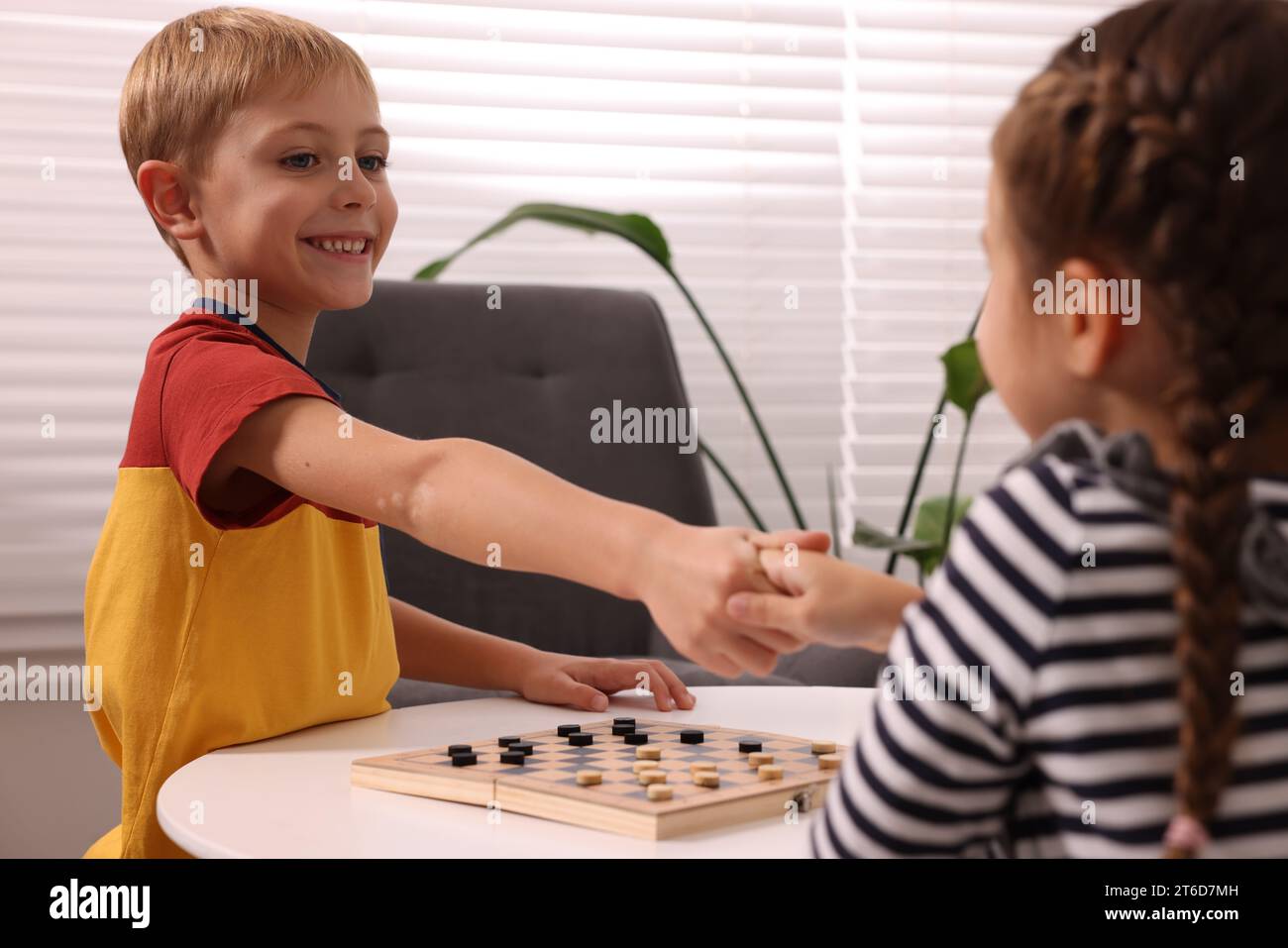Children shaking hands after playing checkers at coffee table indoors ...