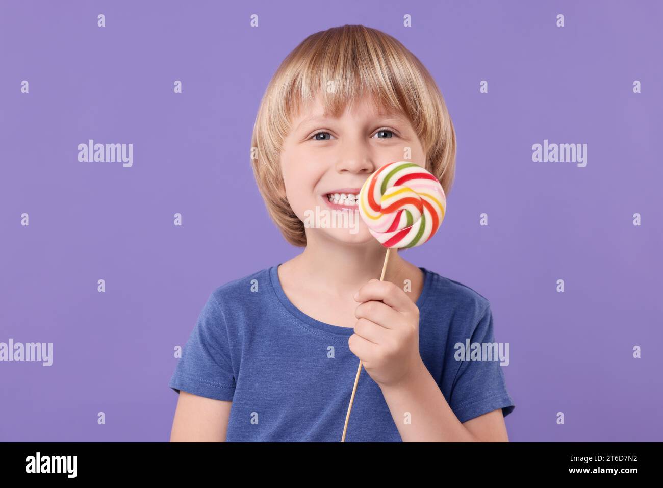 Happy little boy with colorful lollipop swirl on violet background ...