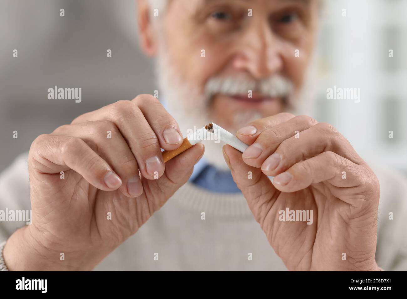Stop smoking concept. Senior man breaking cigarette on blurred ...