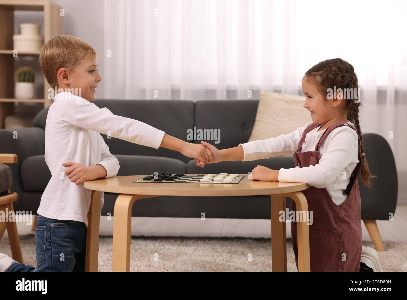 Happy children shaking hands after playing checkers at coffee table in ...