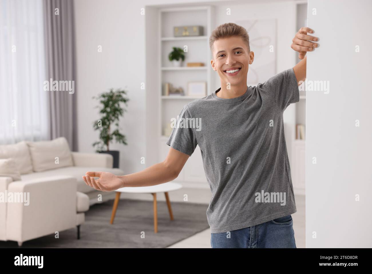 Happy man welcoming near white wall at home. Invitation to come in room ...