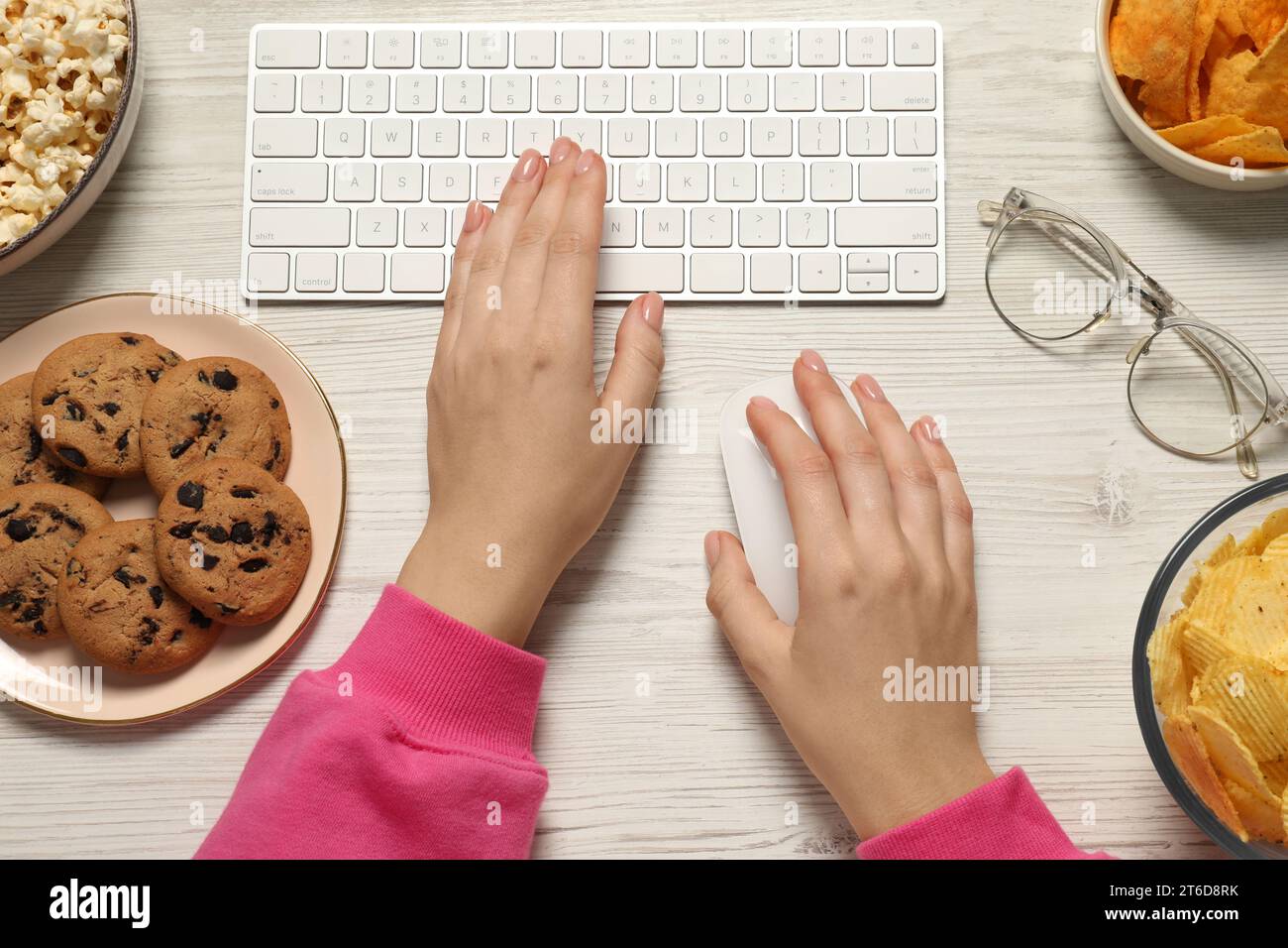 Bad eating habits. Woman working on computer at white wooden table with ...