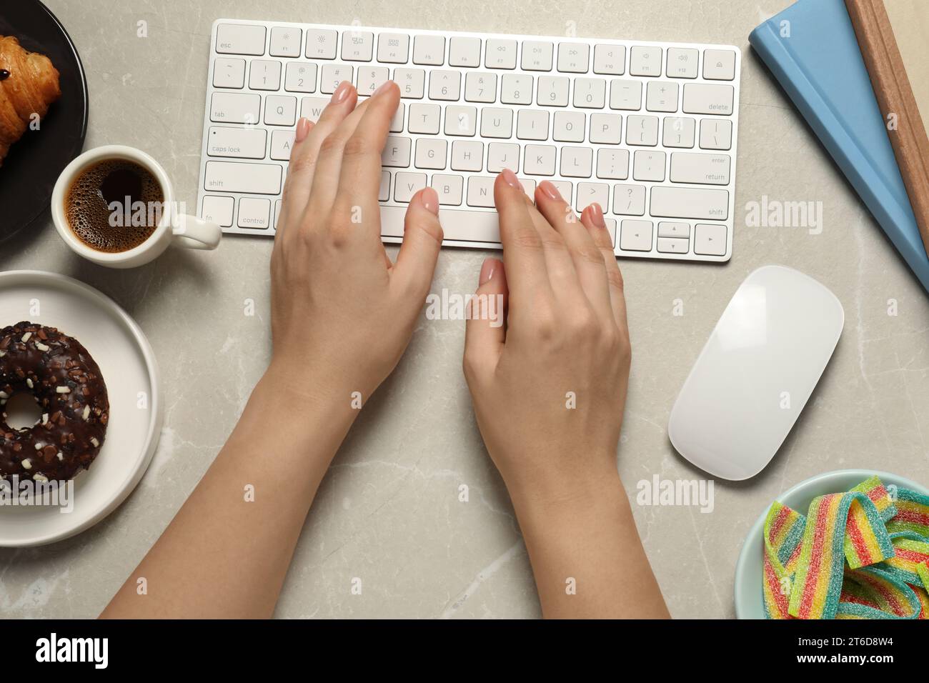 Bad eating habits. Woman working on computer at light grey marble table ...