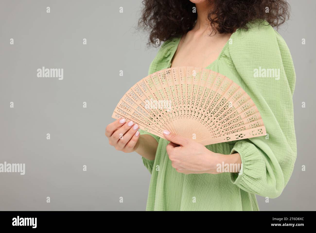 Woman holding hand fan on light grey background, closeup. Space for ...