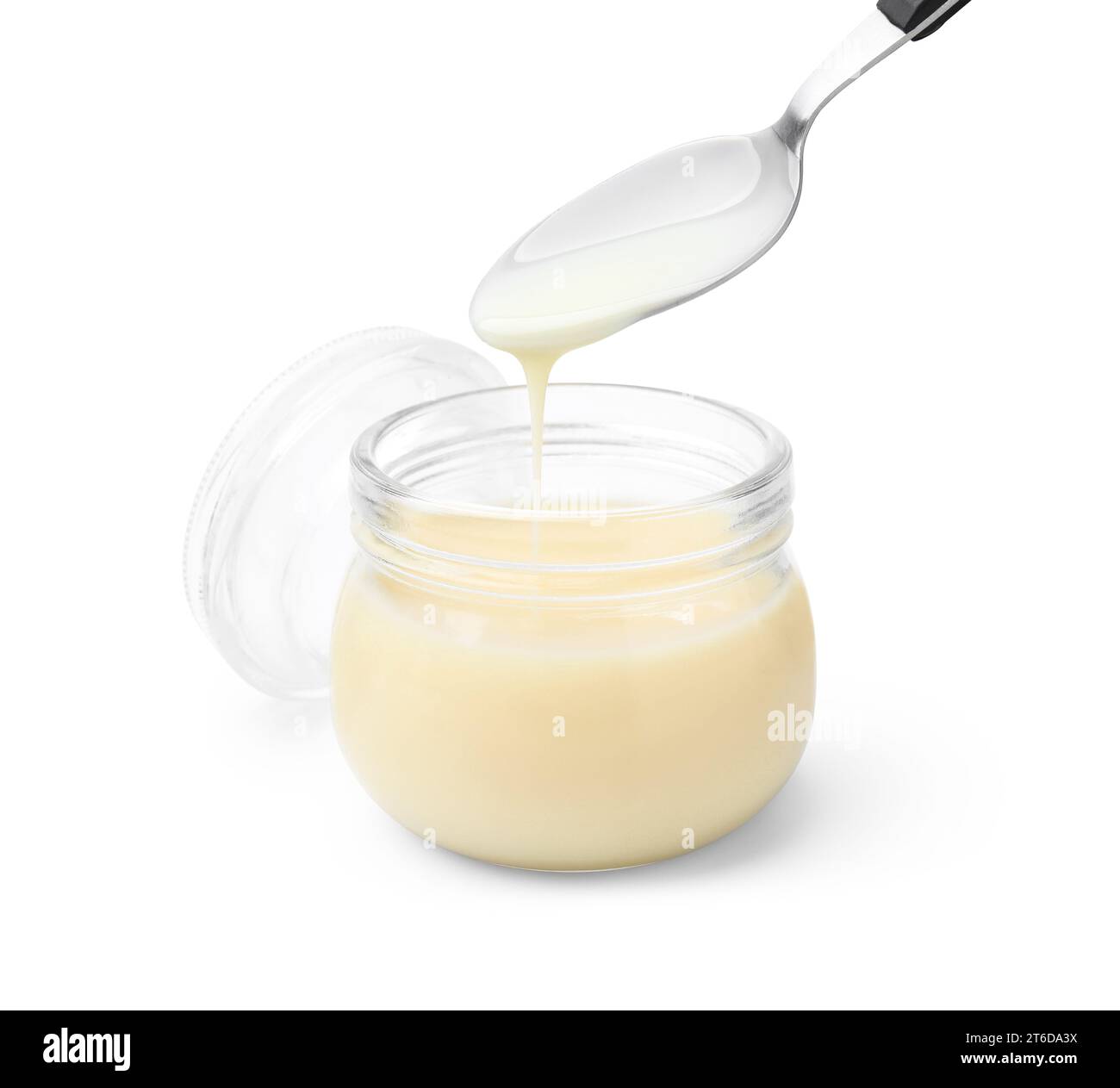 Condensed milk flowing down from spoon into jar isolated on white Stock ...