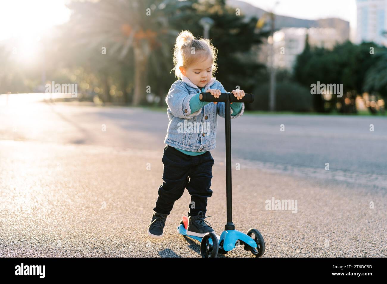 Little girl rides a scooter, pushing off with her foot on the road ...